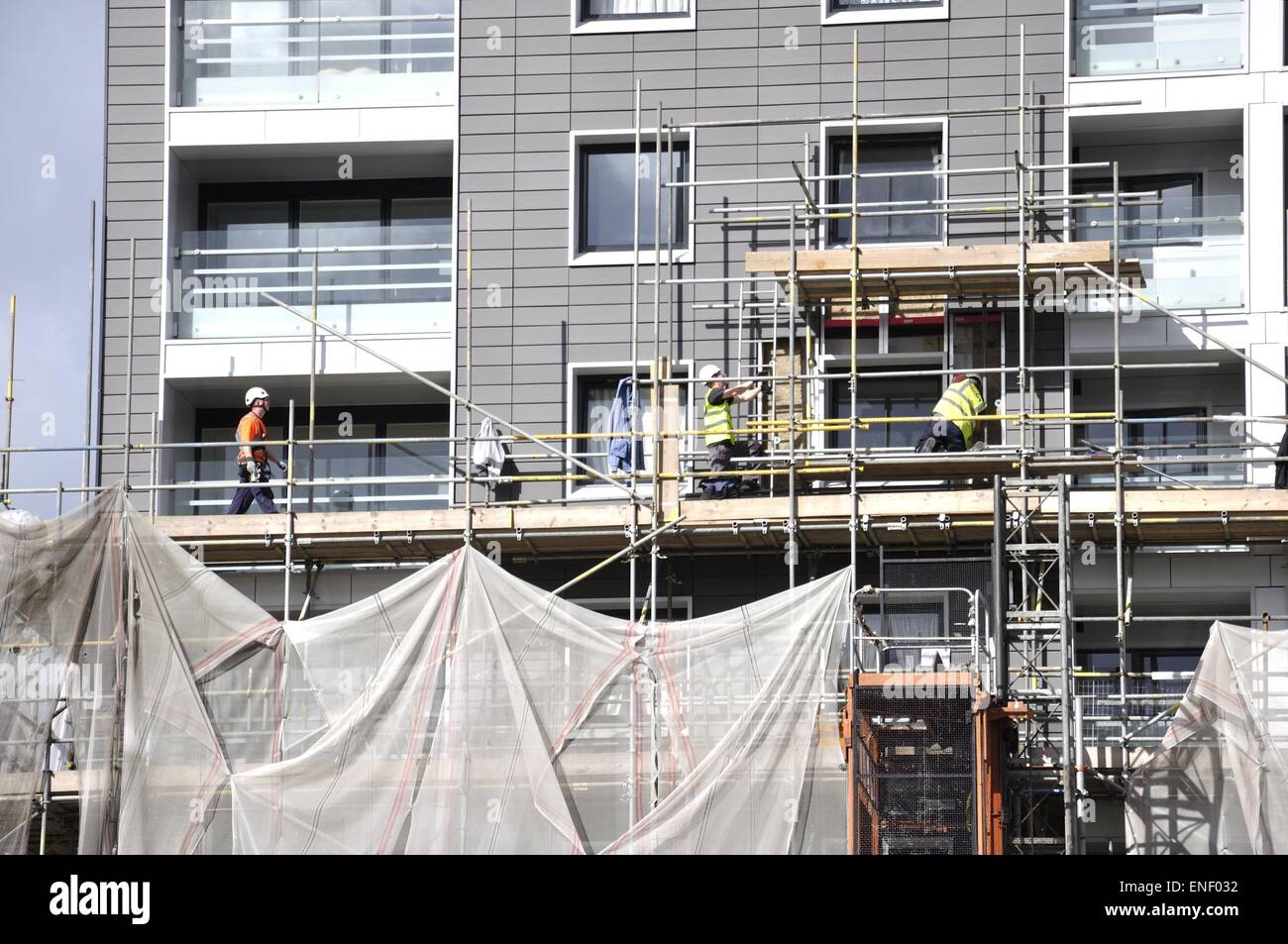 Workmen in safety gear removing scaffolding and protective sheeting ...
