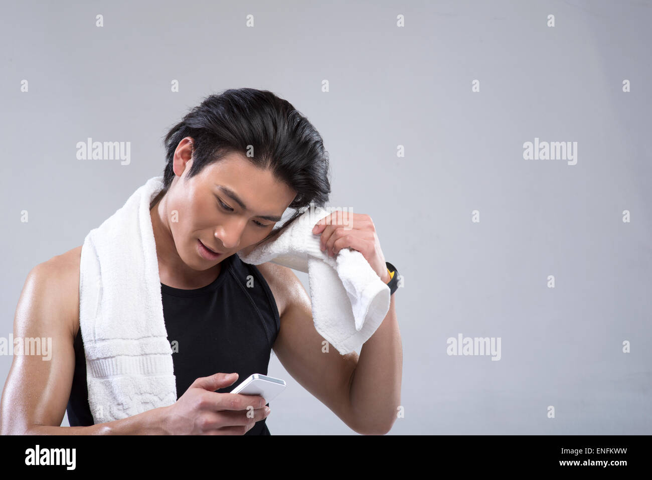 Young man looking at smart phone, wiping forehead with white towel ...