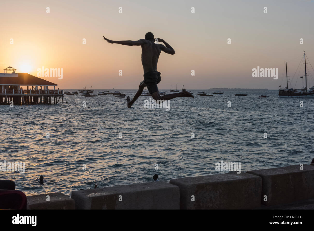 Young man jumping into the water, silhouette, at sunset, wharf ...