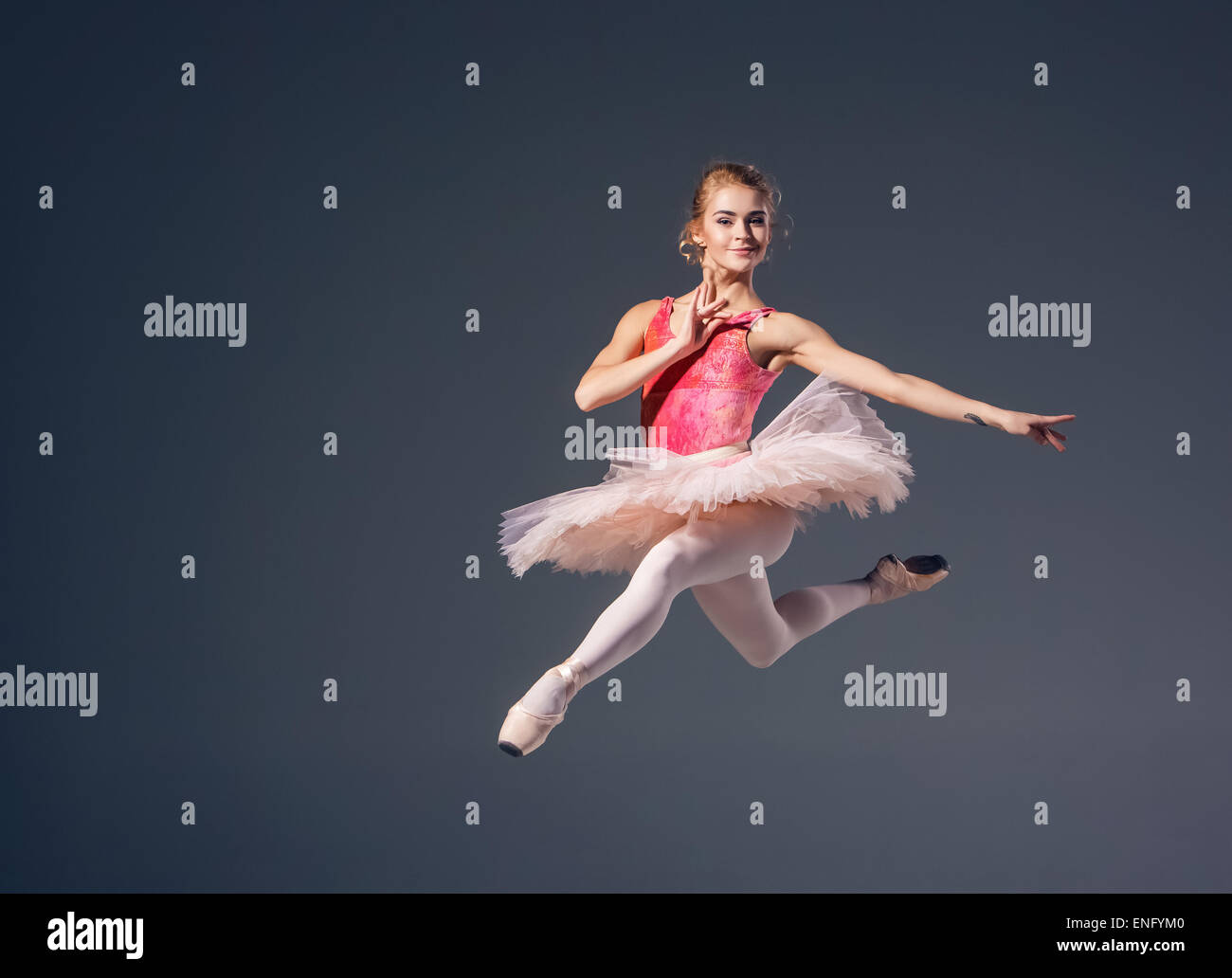 Beautiful female ballet dancer on a grey background. Ballerina is wearing pink tutu and pointe ...