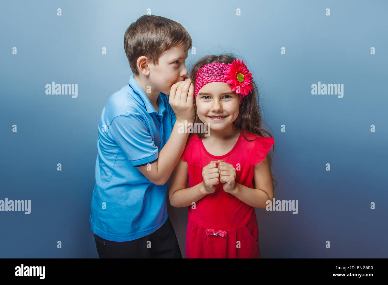 Teen boy whispering in the ear of teen girl on a gray background Stock ...