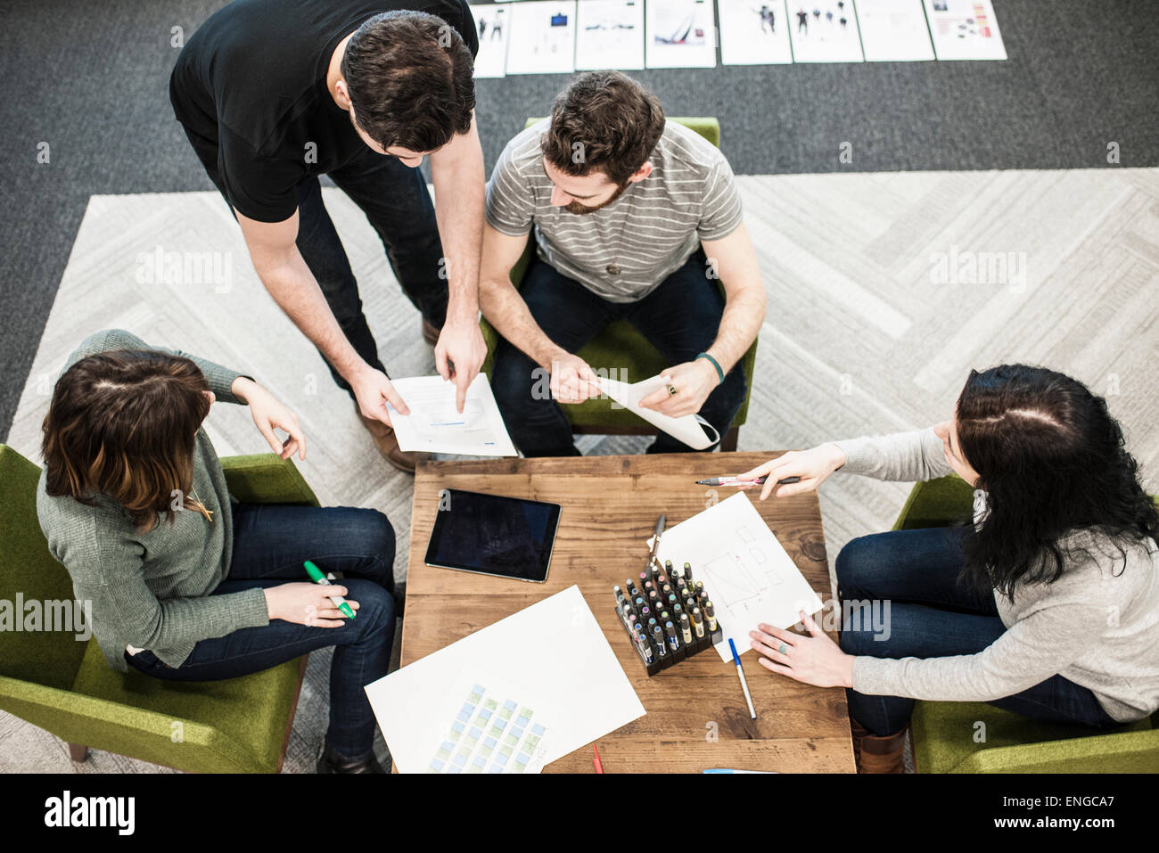 Four people seated at a table using coloured pens on paper, colleagues ...