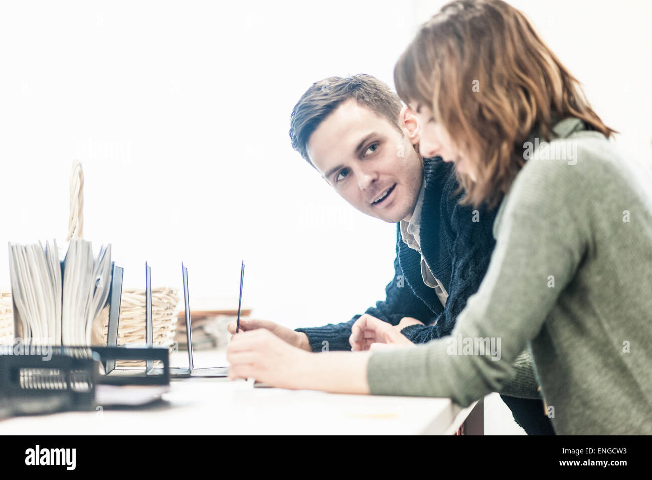 A man and a woman seated side by side talking at a desk in an office ...