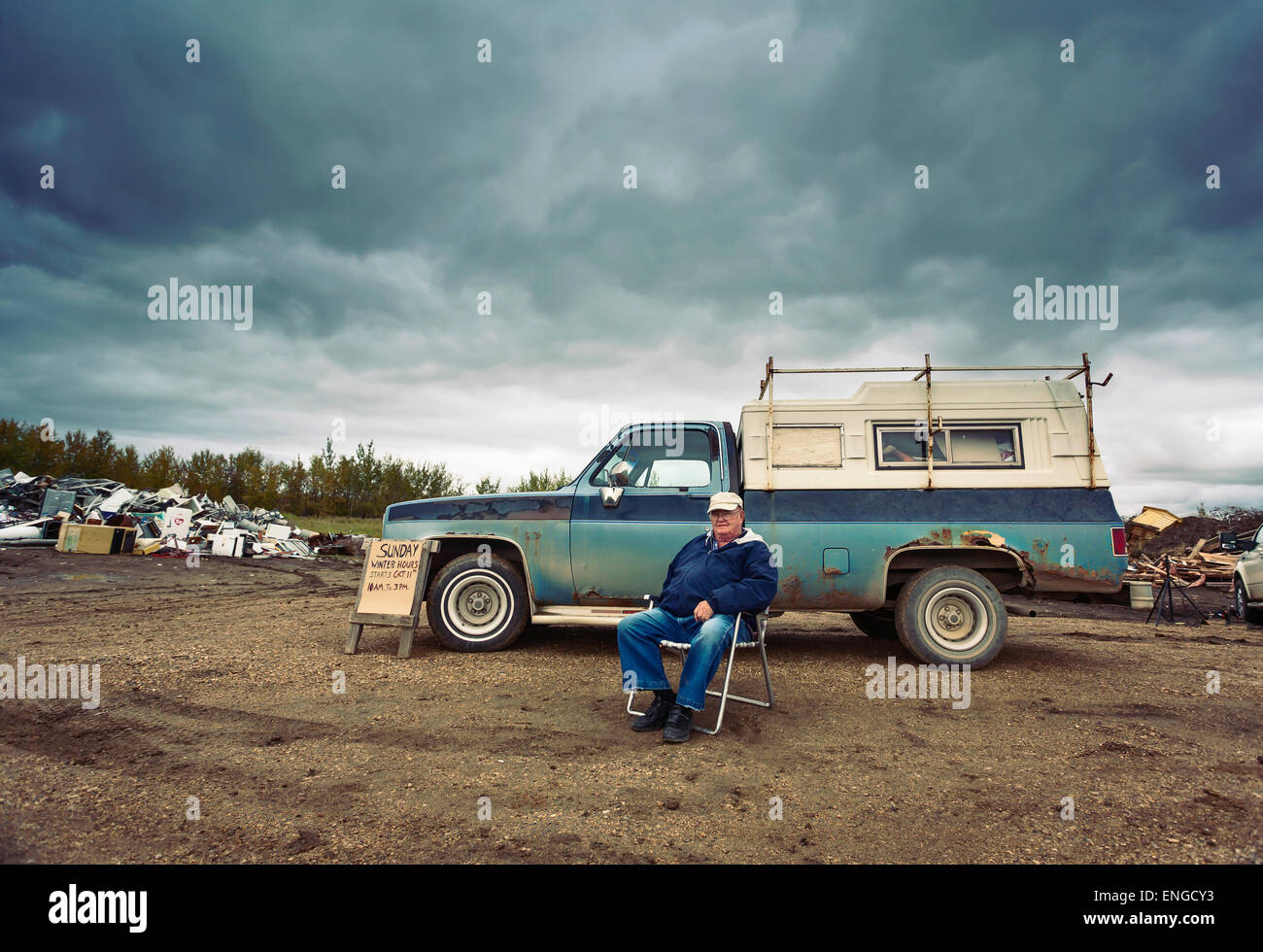 A mature man seated in a chair by his pick up truck. Piles of waste ...