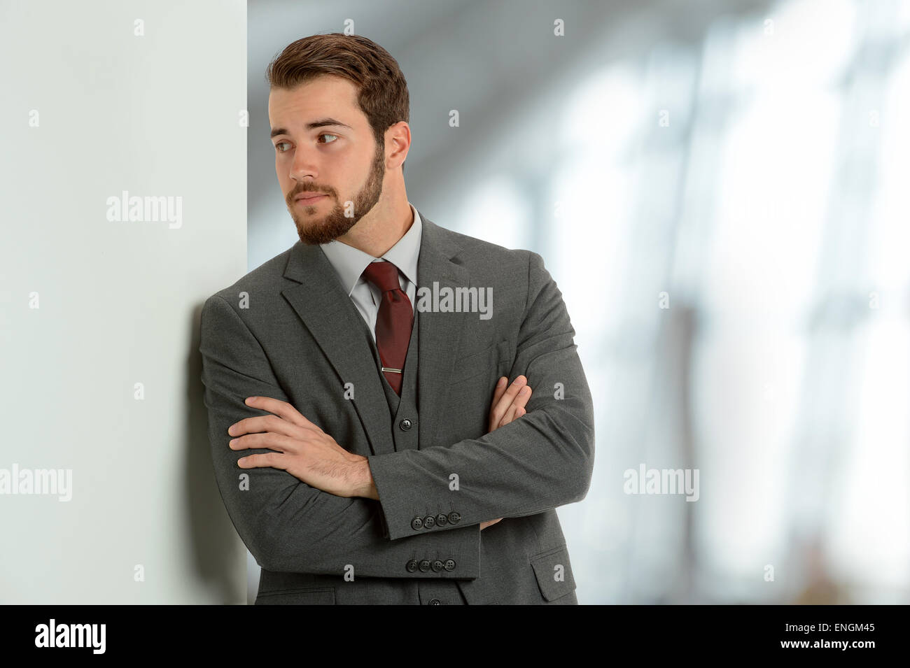 Portrait of young businessman leaning on wall inside office building ...