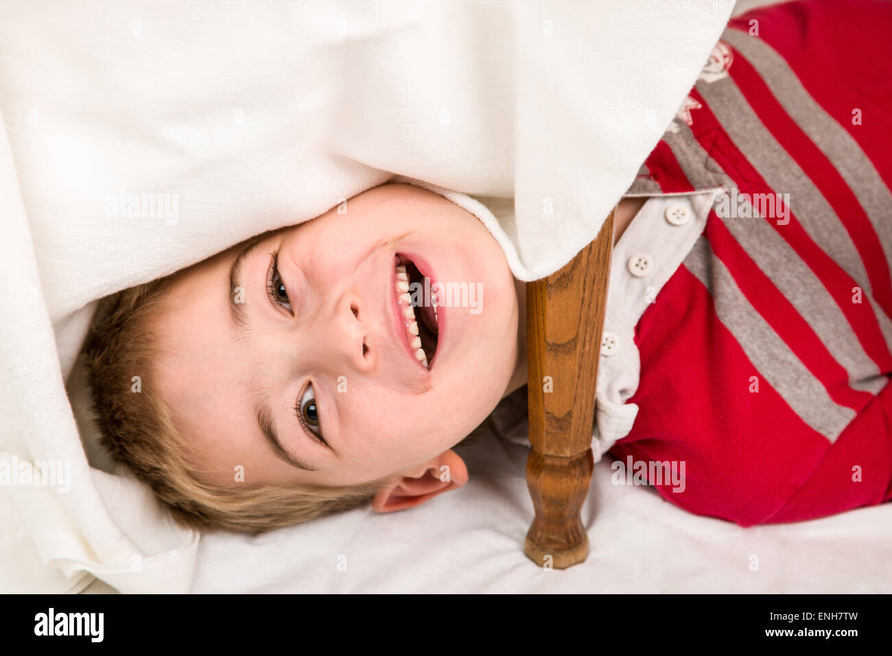 Six year old boy having fun playing and hiding under a covered table ...