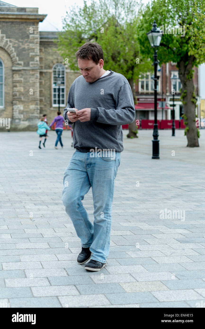 Young man walking whilst using mobile phone Stock Photo - Alamy