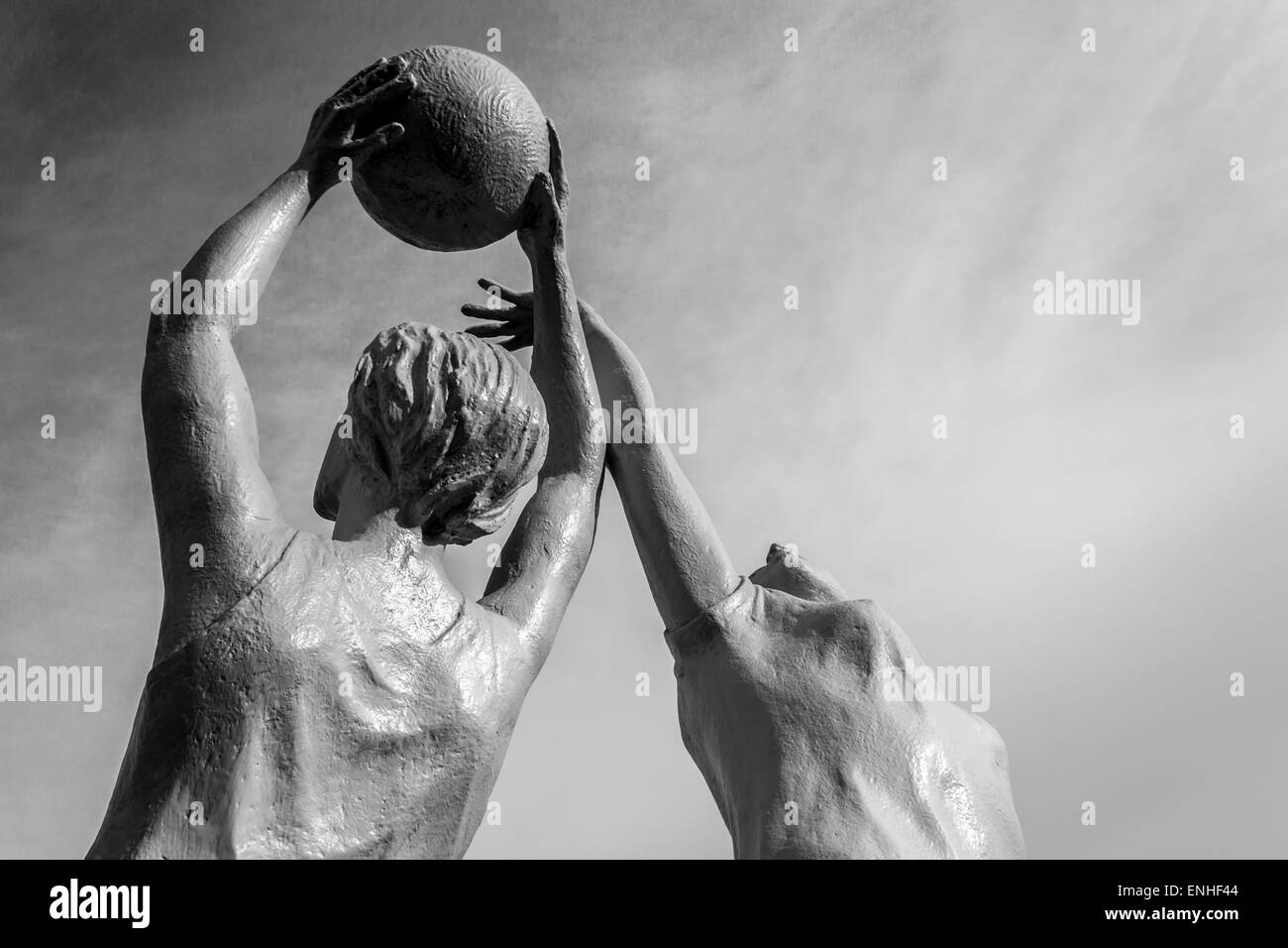 White stone statue of two women playing netball against a blue sky ...