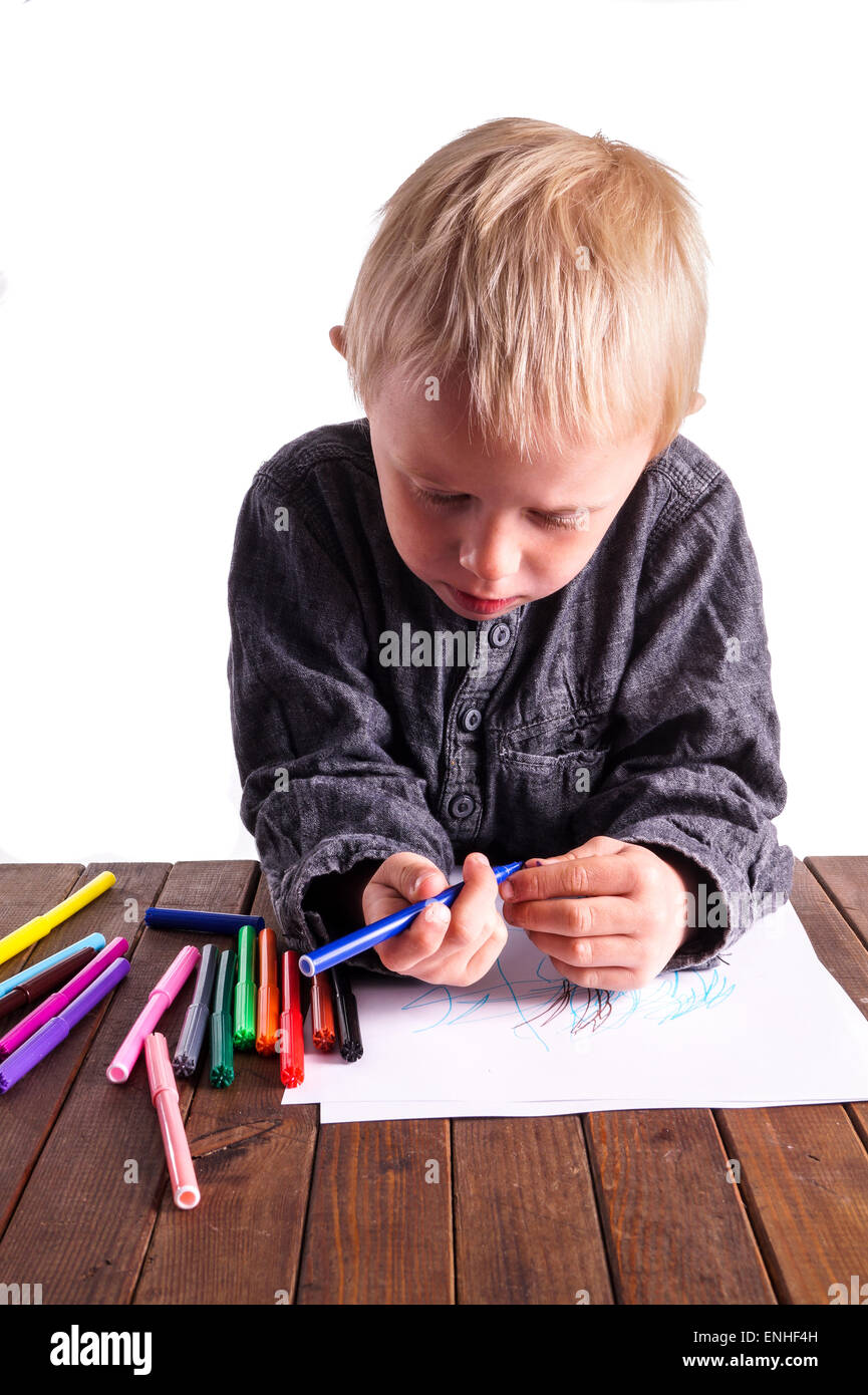 Little boy draws a drawing. He has many markers and are very focused on ...