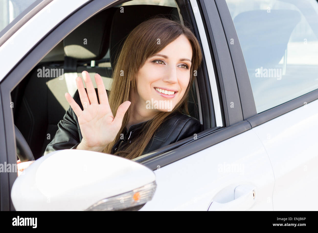 Young smiling woman greeting with hand from car. Cheerful caucasian ...