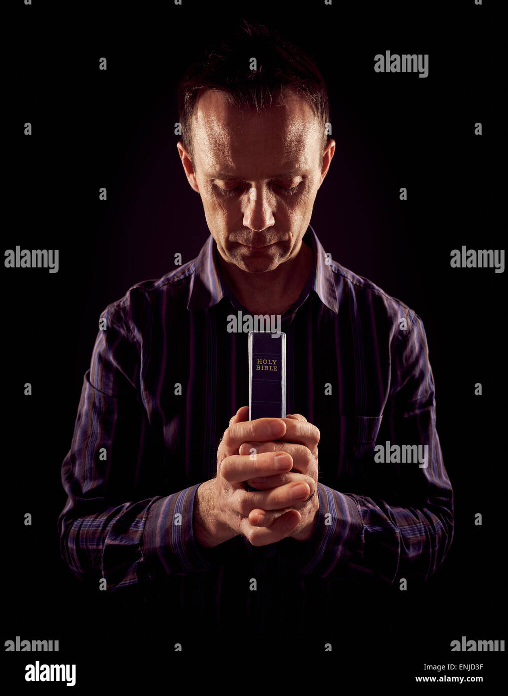 A front view of a man praying in the dark with light shining on both ...
