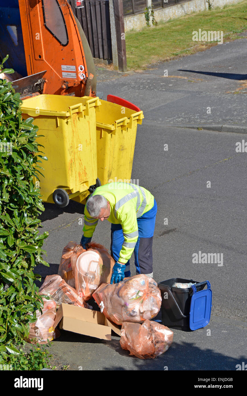 Dustman worker at back rear of refuse dustcart truck at work picking up ...