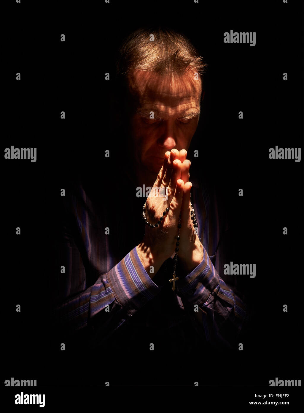 A front view of a man praying in the dark with a ray of sunlight ...