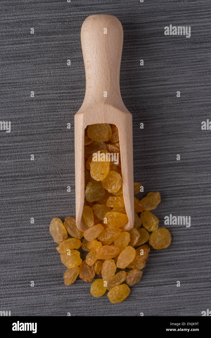 Top view of wooden scoop with golden raisins against grey vinyl ...
