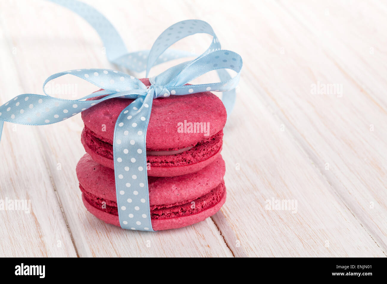 Red macarons with blue ribbon on white wooden table Stock Photo - Alamy