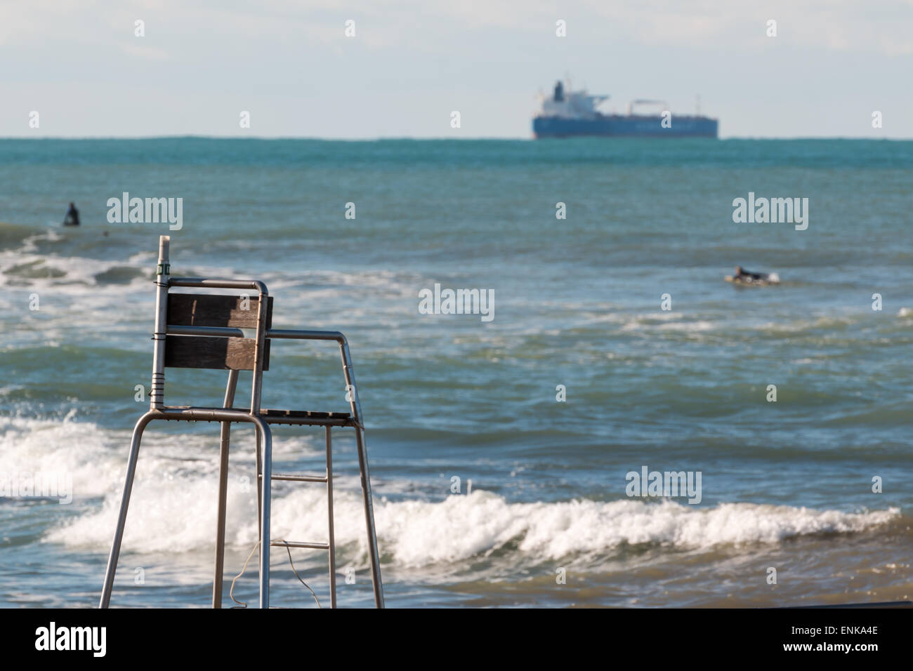 empty lifeguard chair, surfers in sea and container ship in background ...