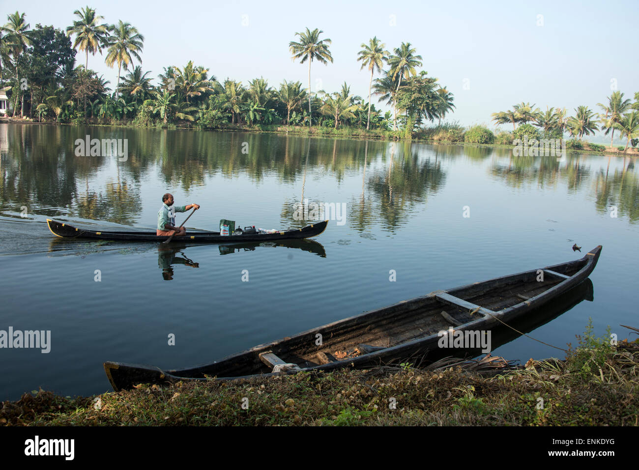 A local villager paddling past a moored canoe on the banks of the ...
