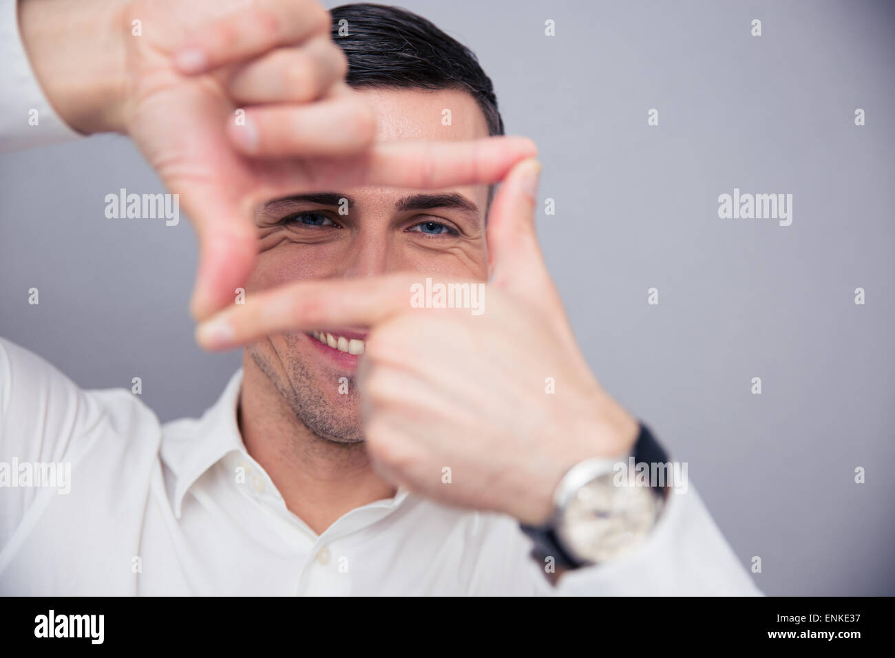 Businessman making frame with fingers over gray background and looking ...