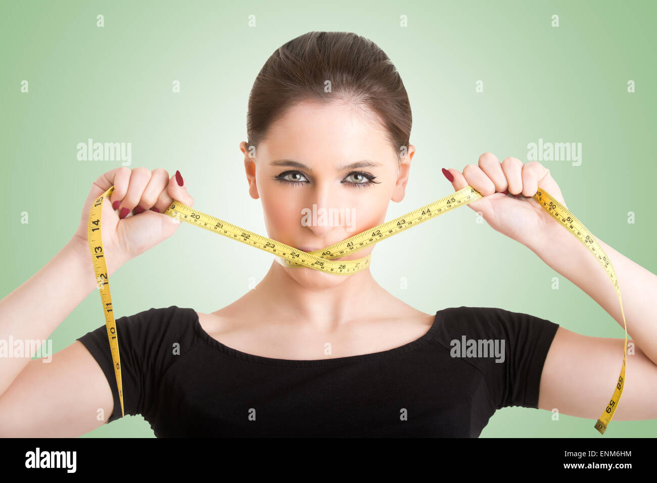 Woman with a yellow measuring tape around her mouth, isolated in green ...