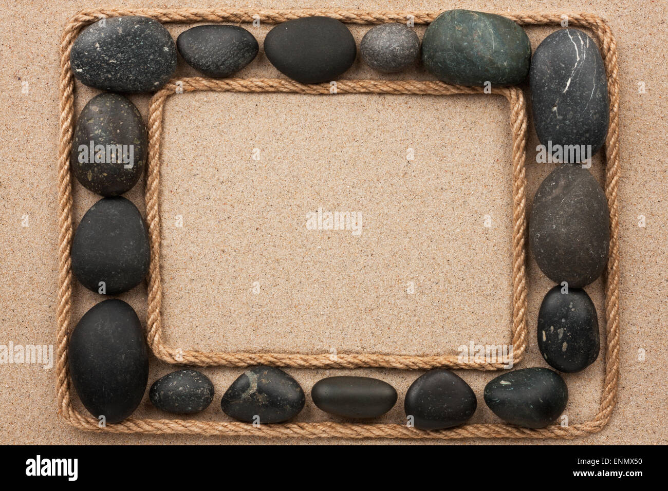 Beautiful frame with rope and black stones on sand, as a background ...