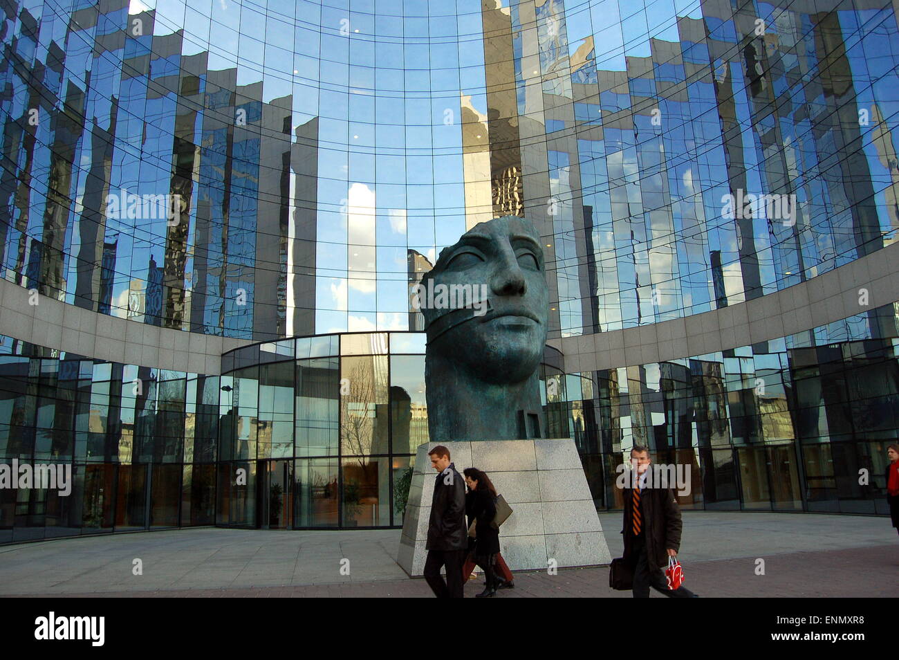 A bronze statue of a man's head surrounded by a modern, glass office ...