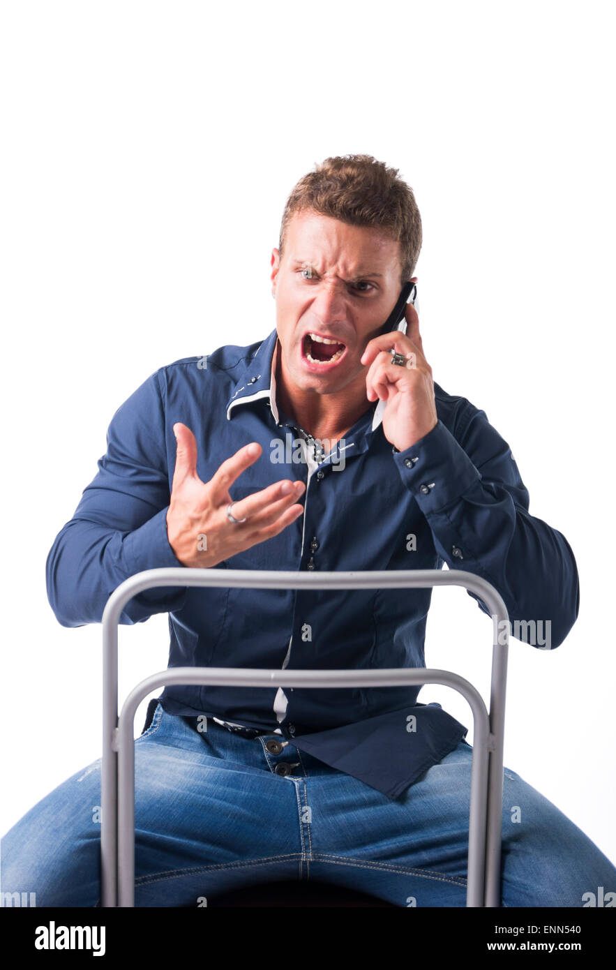 Attractive young man sitting and screaming during phone conversation ...