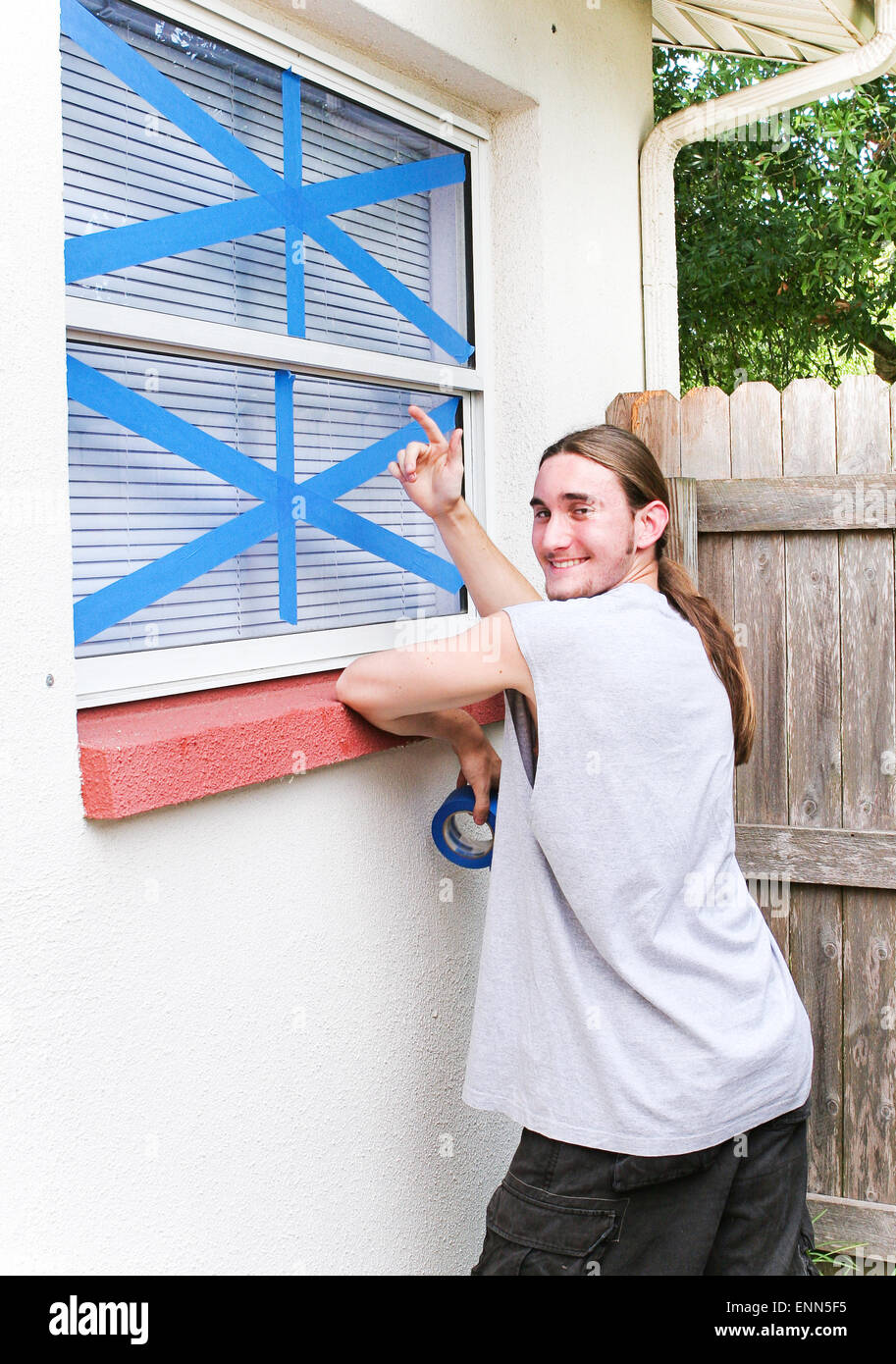 Young man pointing to windows he has taped up to prepare for a ...