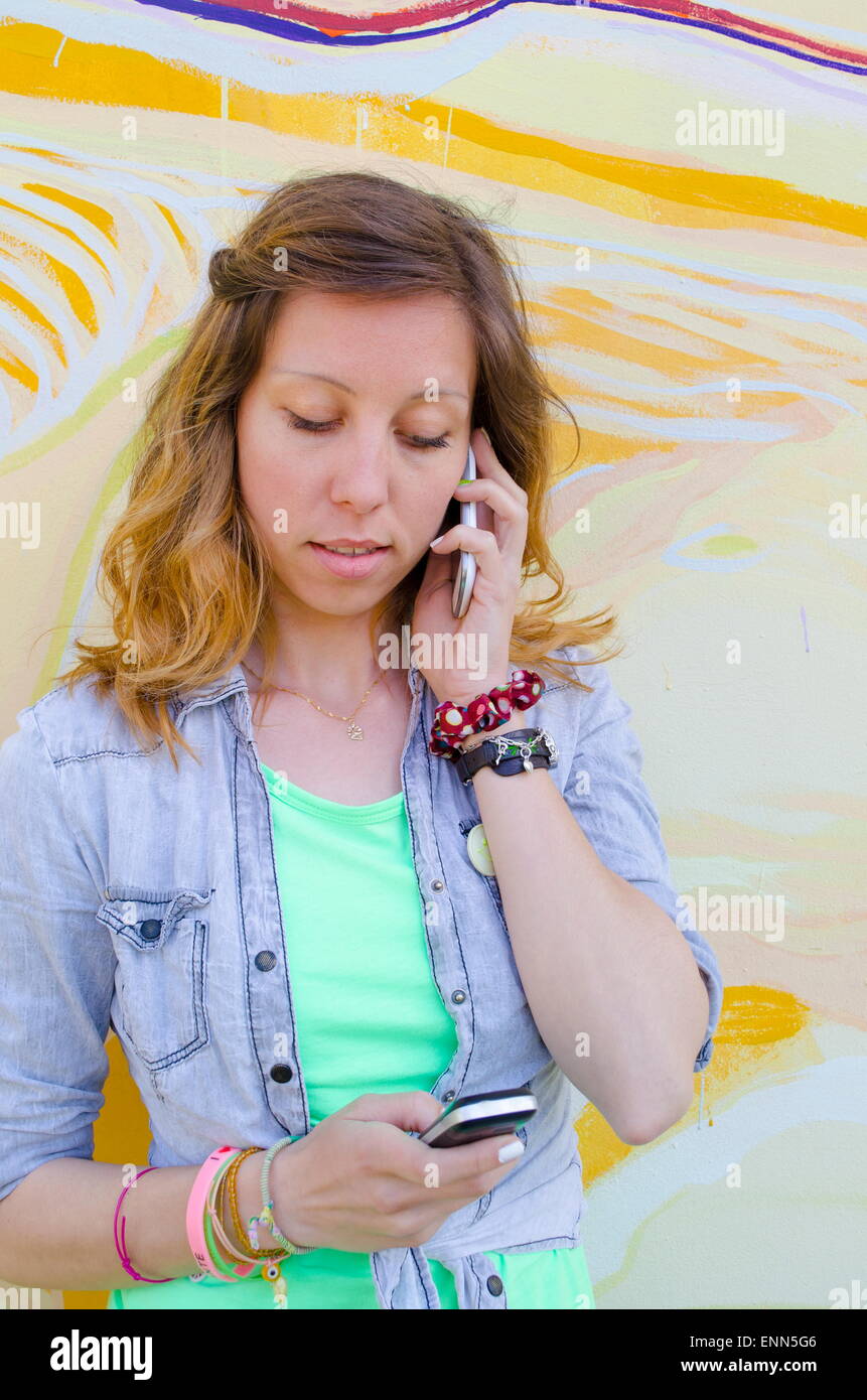 Girl talking on one phone while reading a text message against a ...