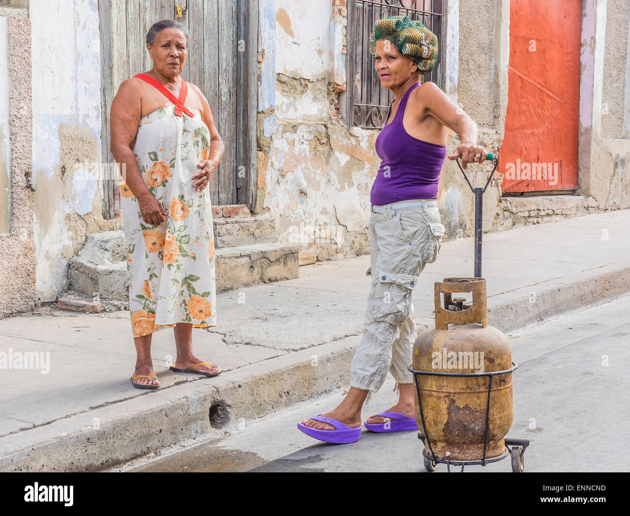 Two Cuban women talking outside, one with hair curlers in her hair and ...