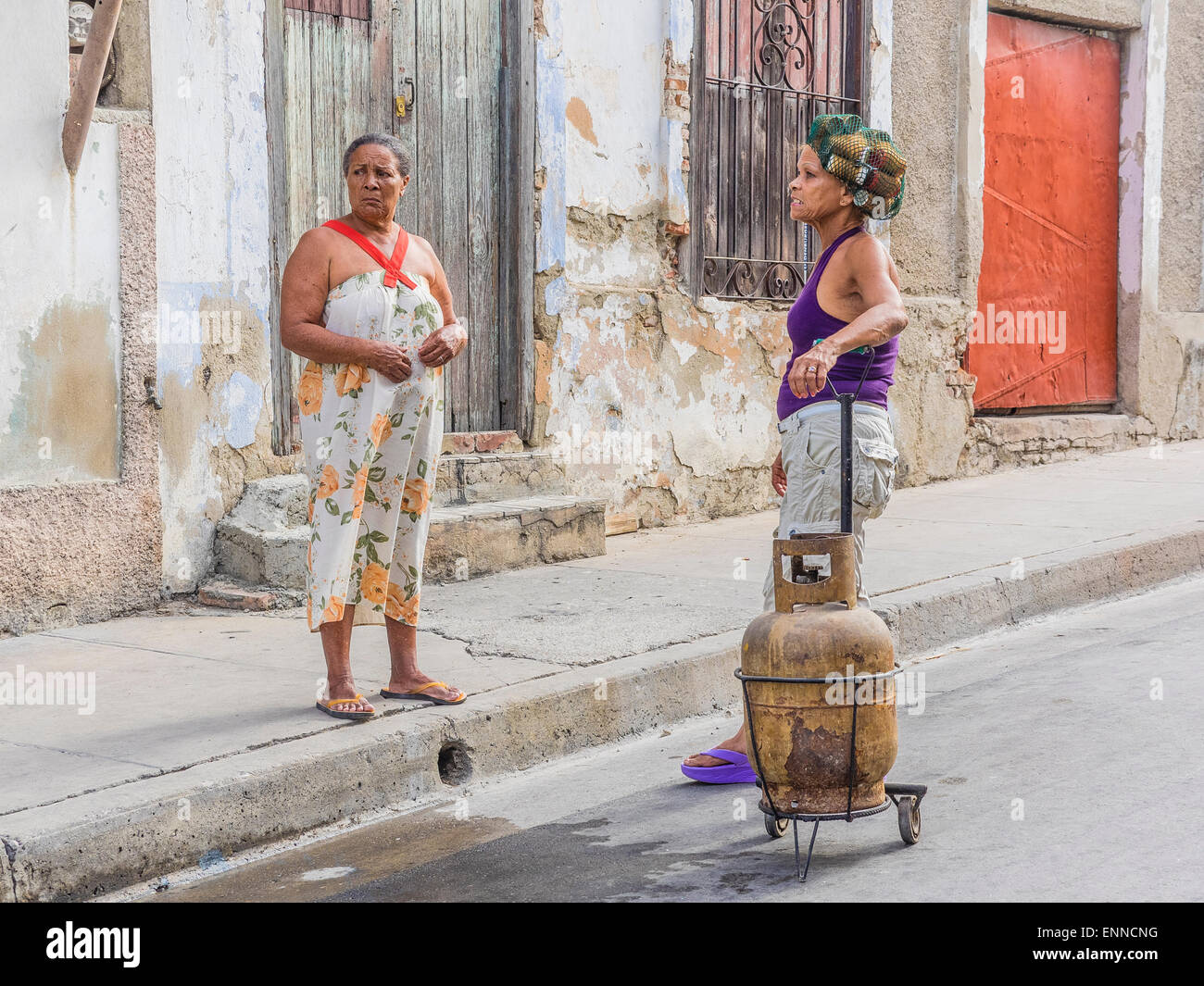 Two Cuban women talking outside, one with hair curlers in her hair and ...
