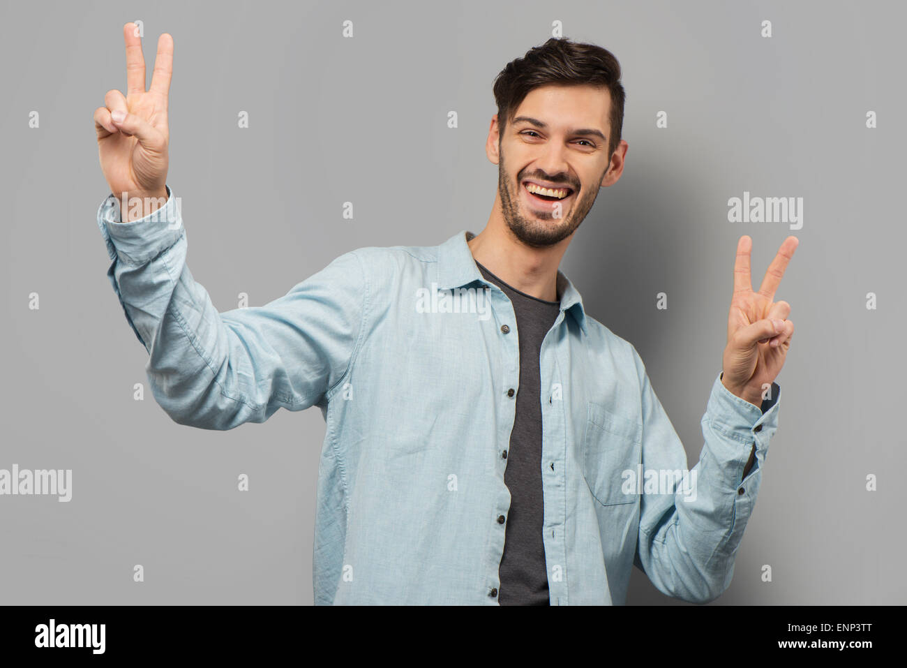 Smiling young man showing victory signs Stock Photo - Alamy