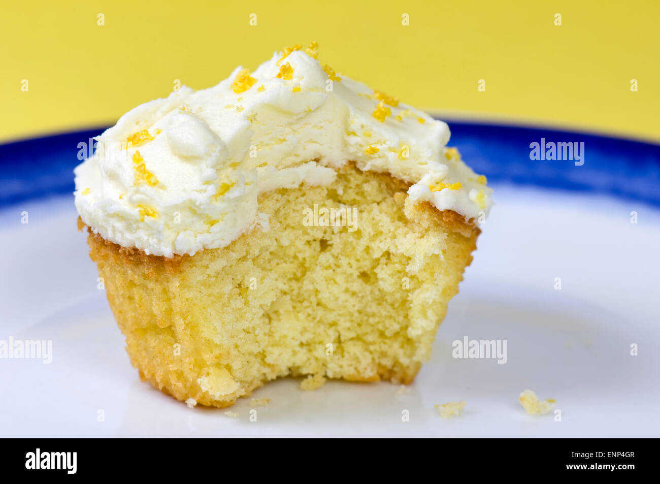 Lemon cupcake with a bite taken out of, on a white and blue plate and a ...
