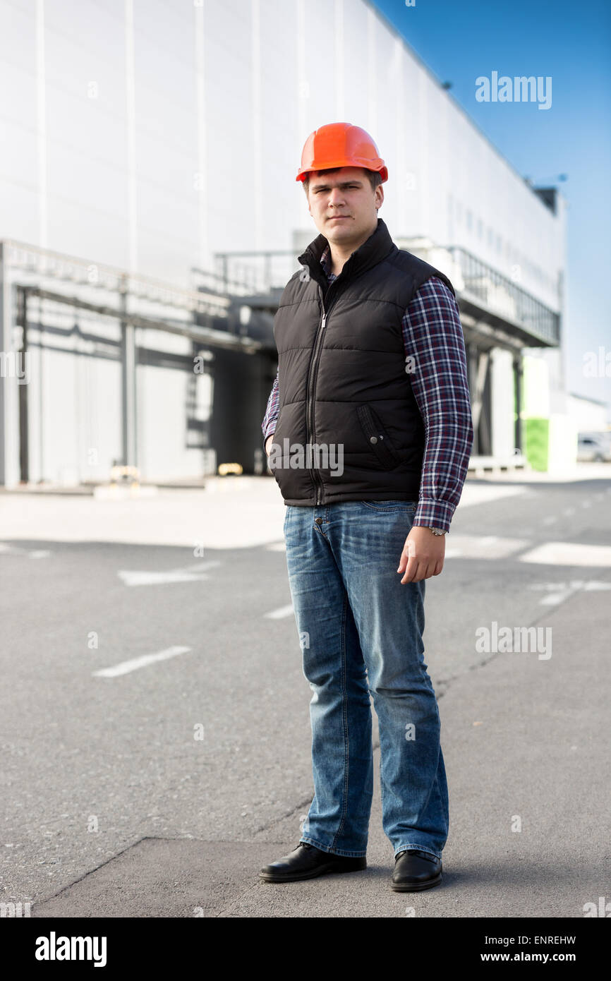 Full length portrait of handsome engineer posing against big warehouse ...