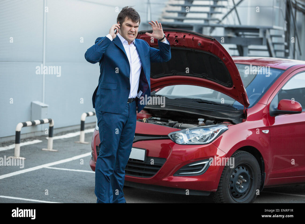 Angry businessman standing next to broken car and calling in service ...