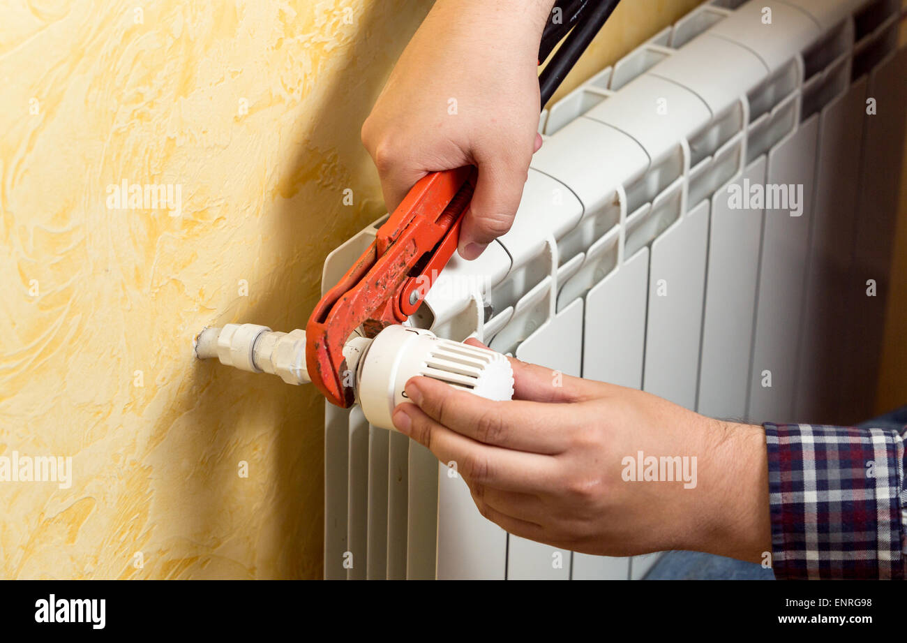 Closeup shot of man installing heating radiator and connecting valve ...