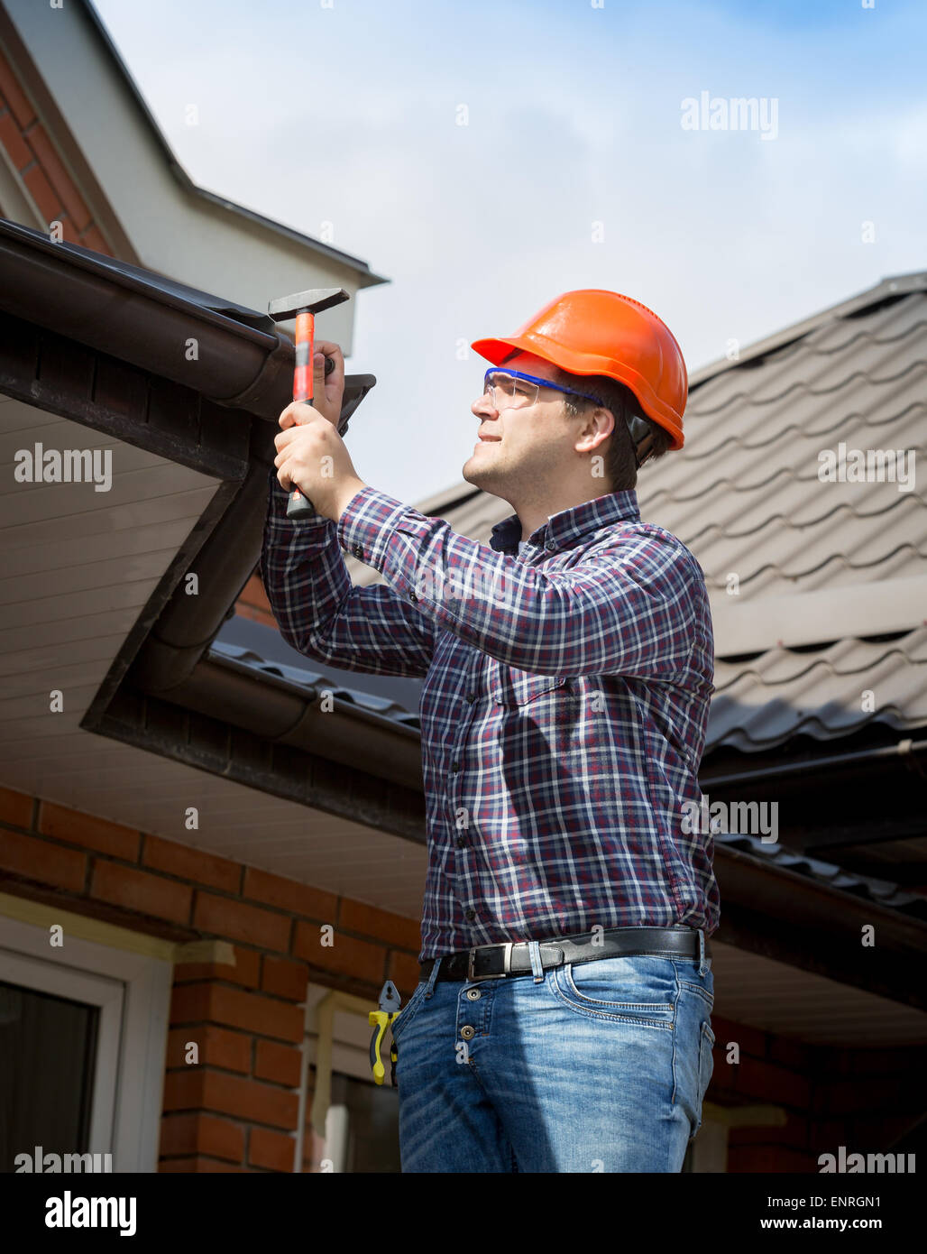 Portrait of young handyman repairing house roof with nails and hammer ...