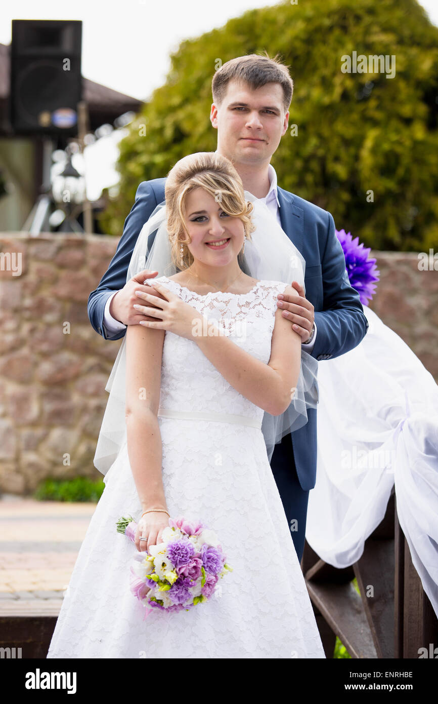 Portrait of young groom hugging cute bride around shoulders Stock Photo ...