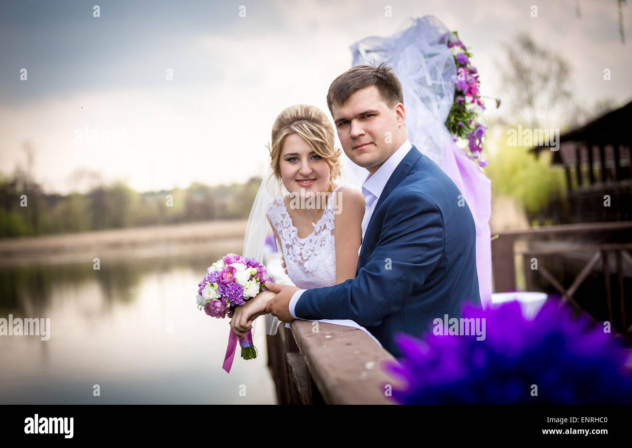 Portrait of happy bride and groom posing on pier at lake Stock Photo ...