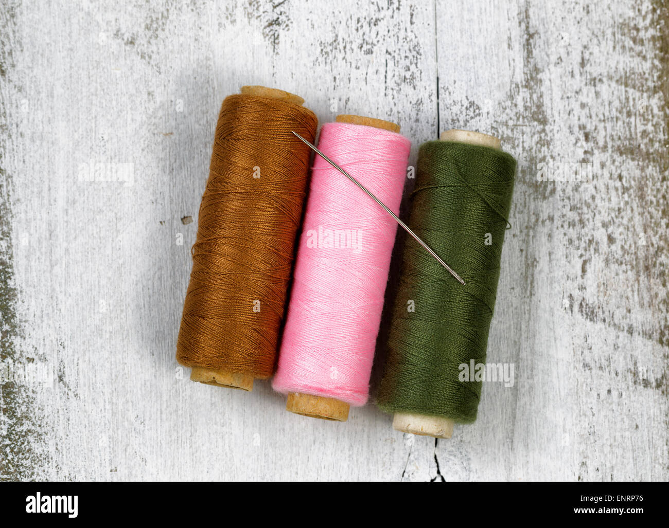 Three spools of different colors of thread, with single needle, on top ...