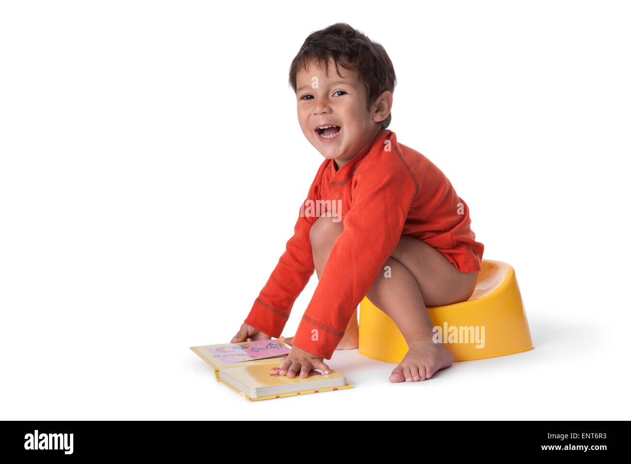Toddler boy sitting on a potty and with a book on white background ...