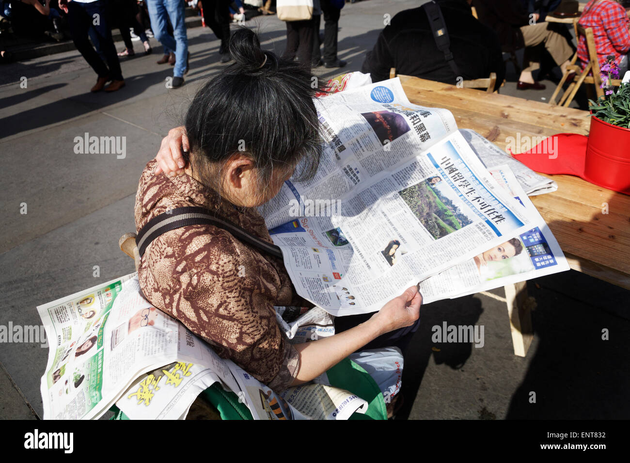 Senior Chinese woman reading Chinese newspaper outdoors. China economy ...