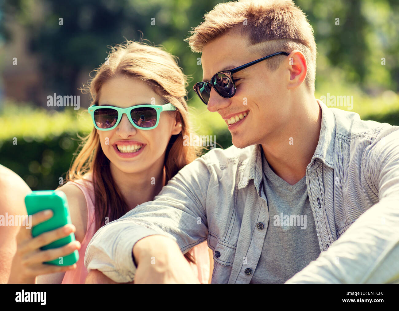 smiling friends with smartphone sitting in park Stock Photo - Alamy