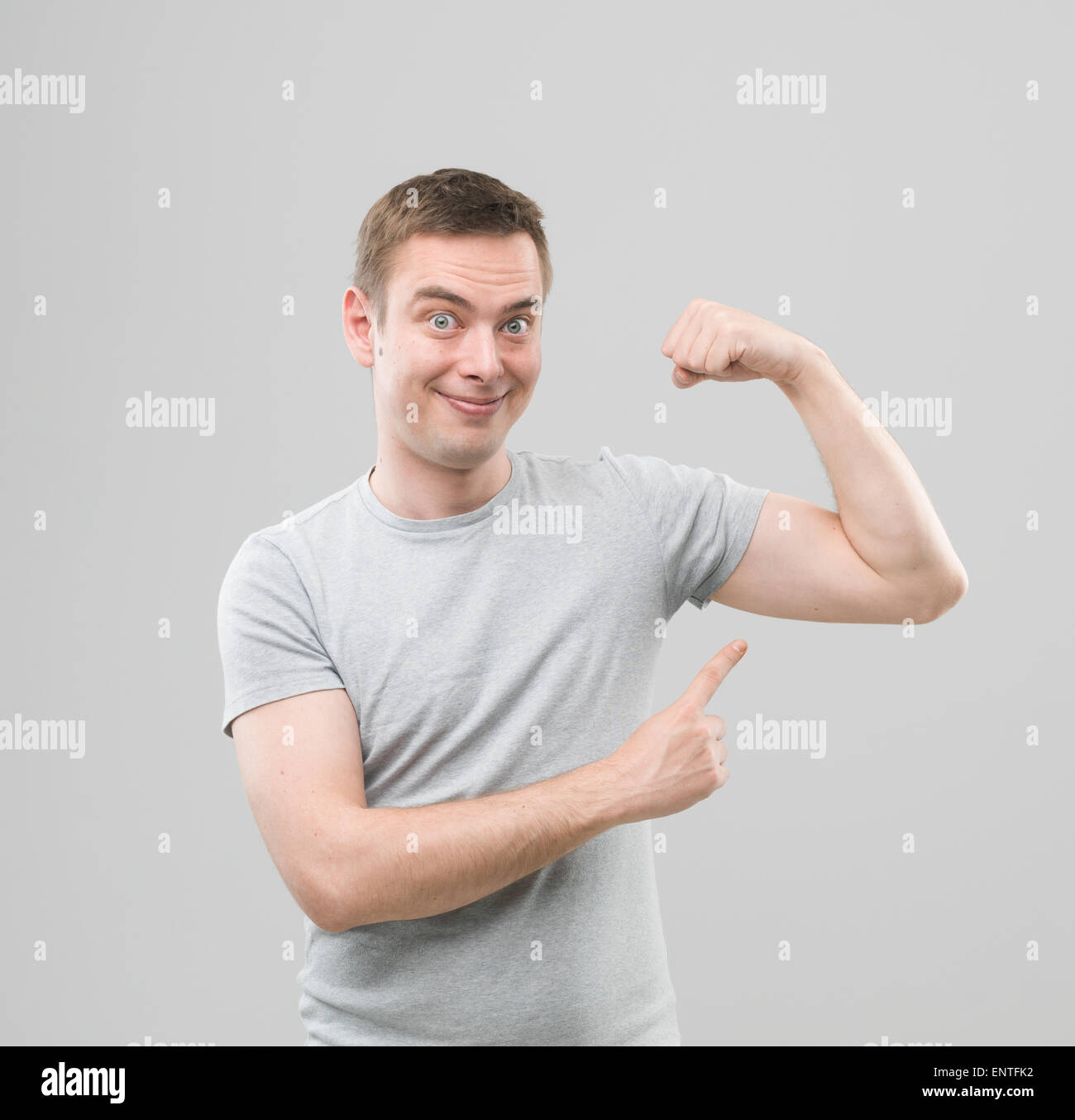 happy caucasian man pointing at his arm muscles and smiling, on grey ...