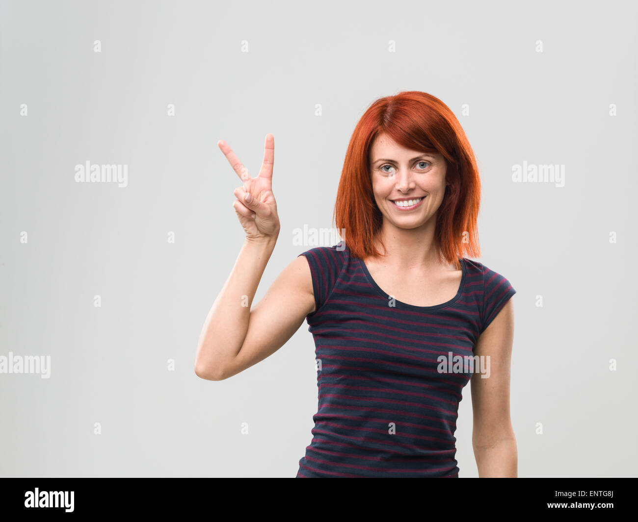 smiling young woman showing peace sign hand gesture, on grey background ...