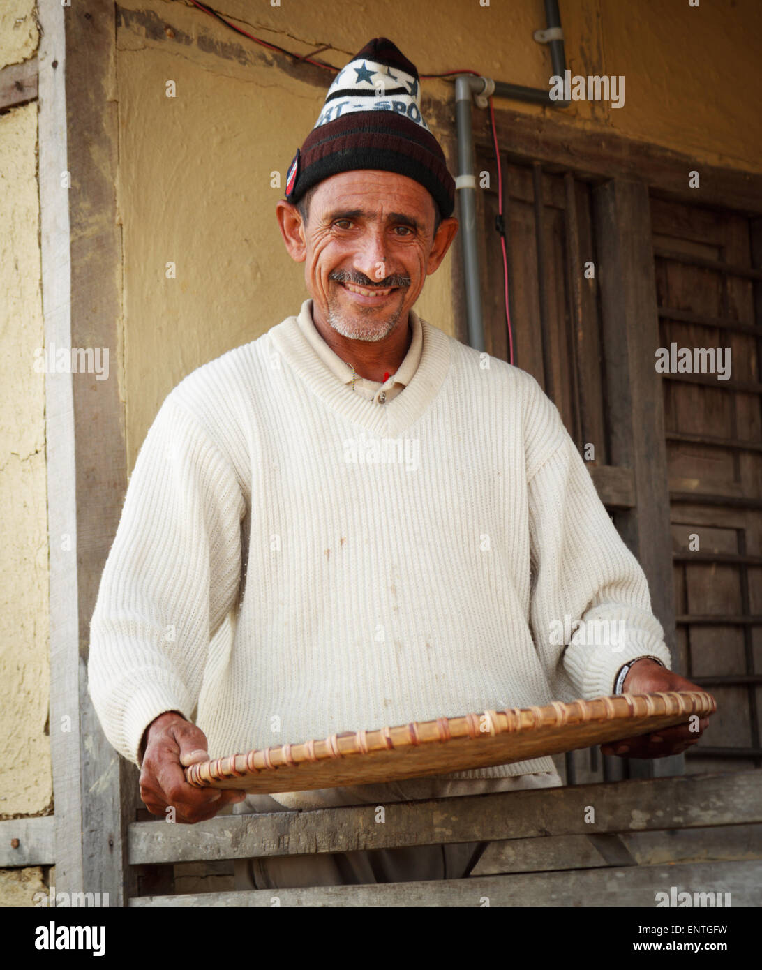 Elderly man sifting rice using a traditional woven cane tray in a ...