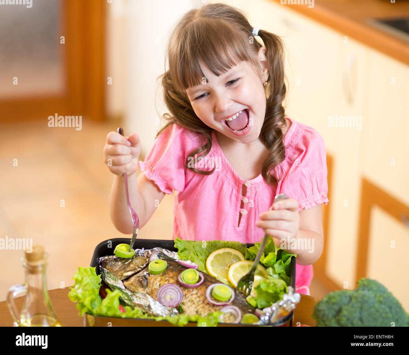 Funny child girl and grilled fish at kitchen. Healthy eating seafood ...