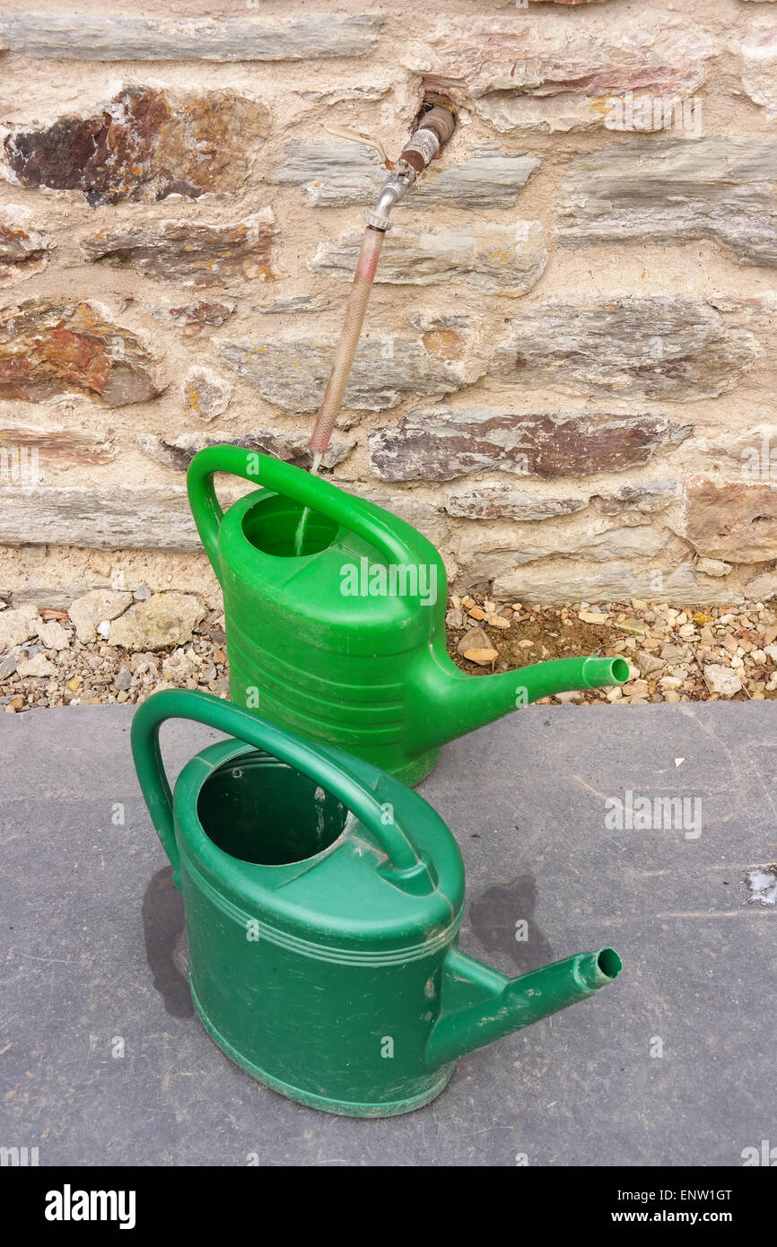 Watering cans filled with a water tap at a slate wall Stock Photo - Alamy