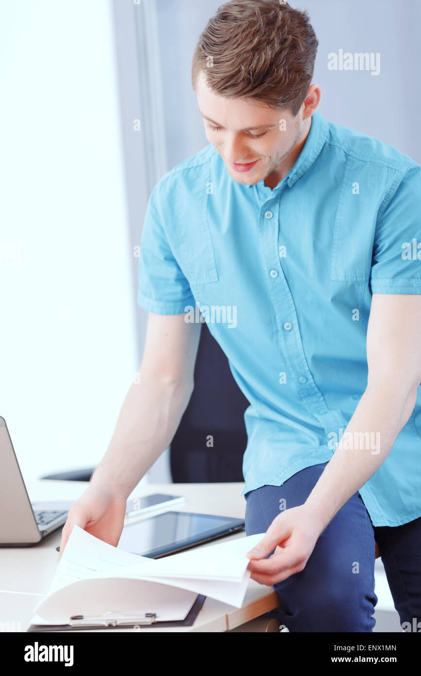 Man sitting on desk and looking through papers Stock Photo - Alamy