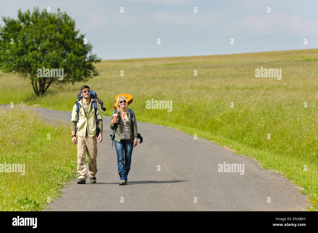 Hiking young couple backpack tramping asphalt road Stock Photo - Alamy