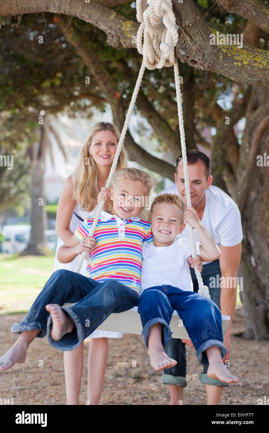 Joyful parents pushing their children on a swing Stock Photo - Alamy